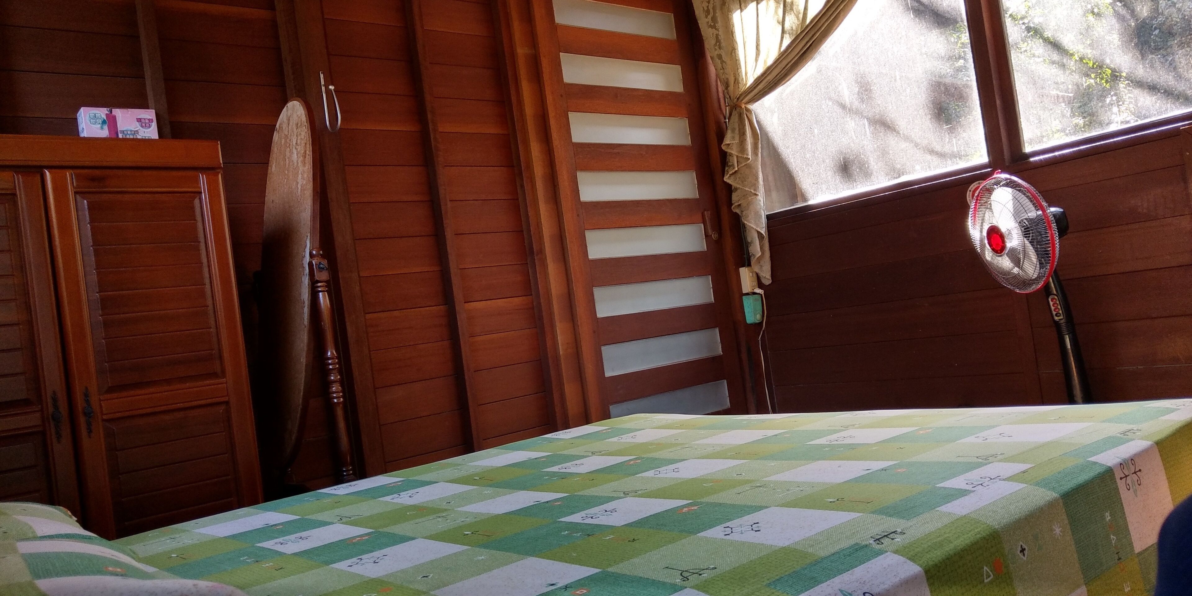 Quarto com toalha xadrez, guarda-roupa de madeira e janela com cortina.