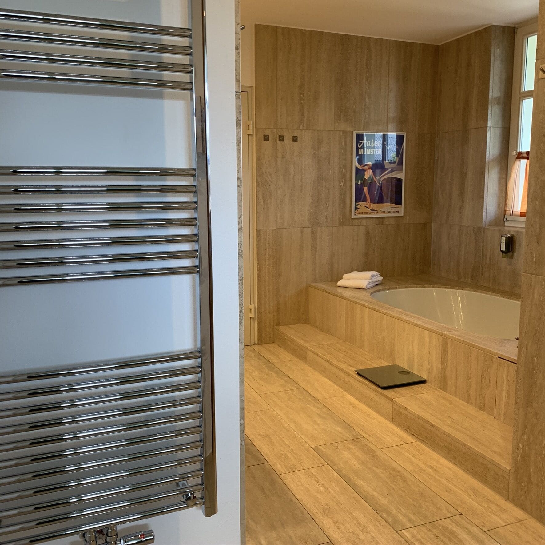 Um banheiro moderno com piso de madeira, box de vidro, banheira e porta-toalhas.