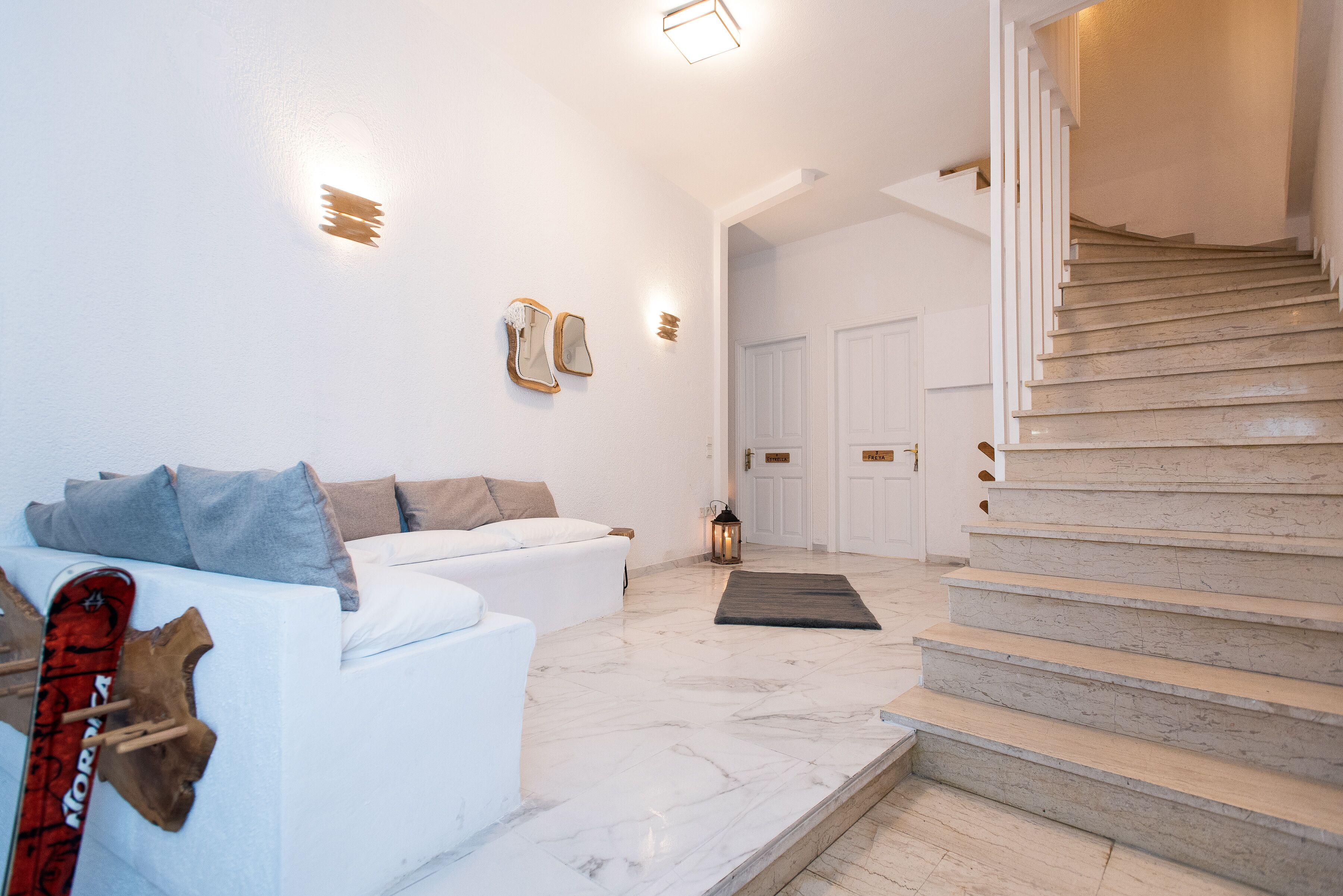 Um interior moderno com um sofá branco, uma escada e uma porta ao fundo.