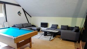 Uma sala de estar aconchegante com mesa de bilhar, sofás, televisão e um tapete pequeno.