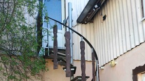 Uma escadaria em espiral com corrimão de metal, fixada a um edifício com fachada bege e uma janela.