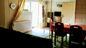 Uma sala de estar com sofá, mesa de jantar com cadeiras, televisão e radiador.