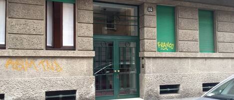 Um edifício com porta verde, número 14, e janela com venezianas verdes. Há grafite visível na parede.