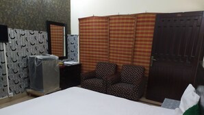 Quarto com cama, uma cadeira, guarda-roupa, espelho e uma mesinha.