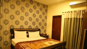 Quarto de hotel com uma cama grande, cabeceira de madeira, parede estampada, porta e cortina.