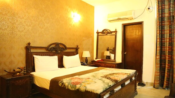 Quarto tradicional com cama de madeira, mesa de cabeceira, espelho e ar condicionado na parede.