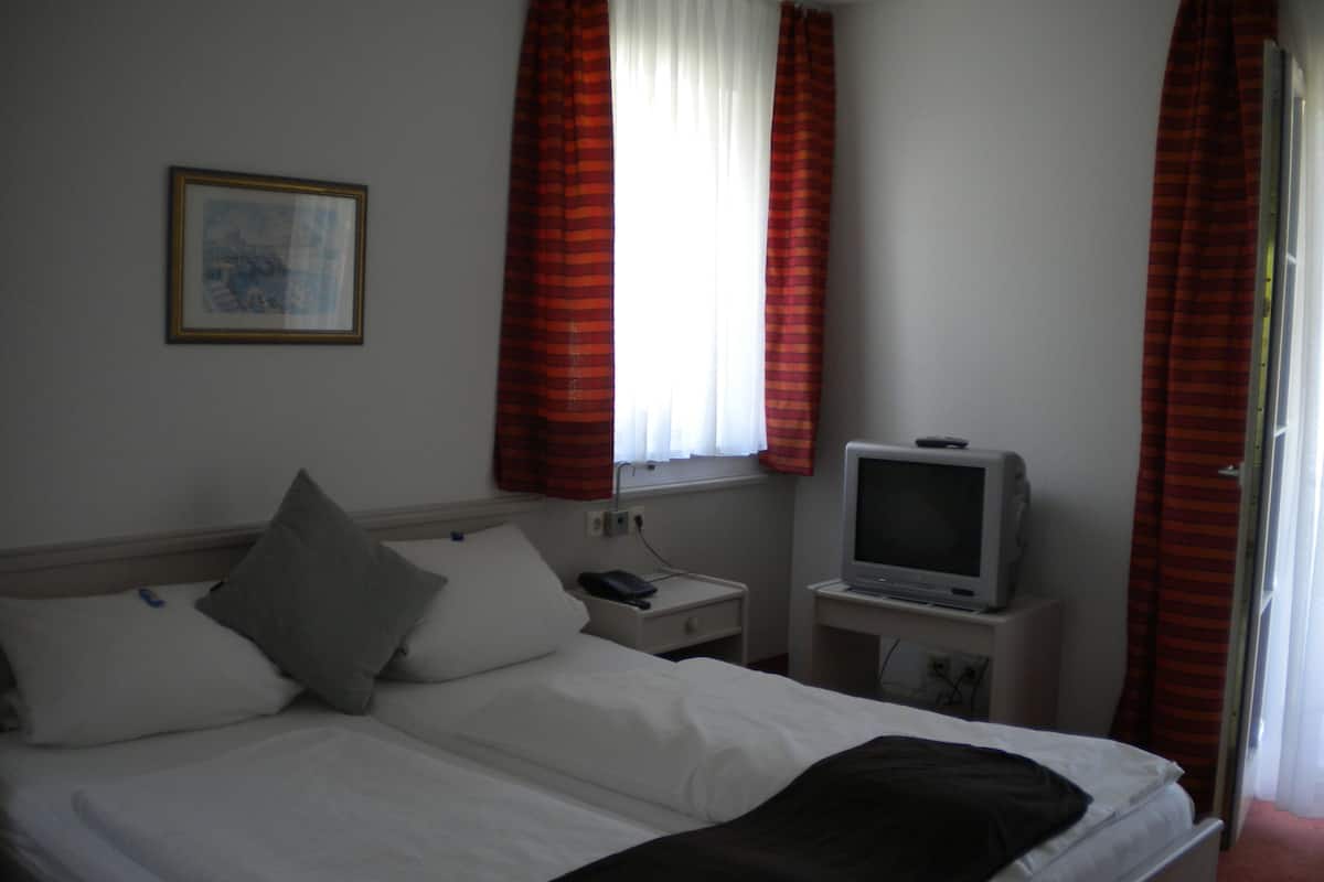 Quarto de hotel com cama, mesa de cabeceira com televisão, telefone e um quadro na parede.