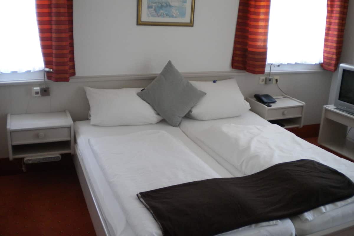 Quarto de hotel com cama, duas mesas de cabeceira, uma televisão e um quadro na parede.