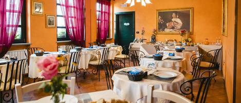 Uma sala de jantar com várias mesas preparadas para o café da manhã, com pão, frutas e bebidas.