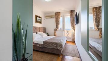 Quarto com cama, planta em vaso, janela com cortinas e televisão de tela plana na parede.