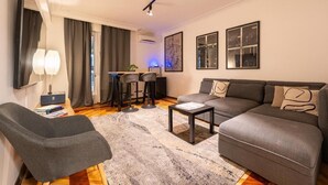 Uma sala de estar moderna com um sofá cinza, uma pequena mesa de centro, uma poltrona cinza e um espaço bar com bancos.