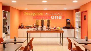 Uma área de café da manhã moderna, com balcão, máquinas de café e uma variedade de frutas.