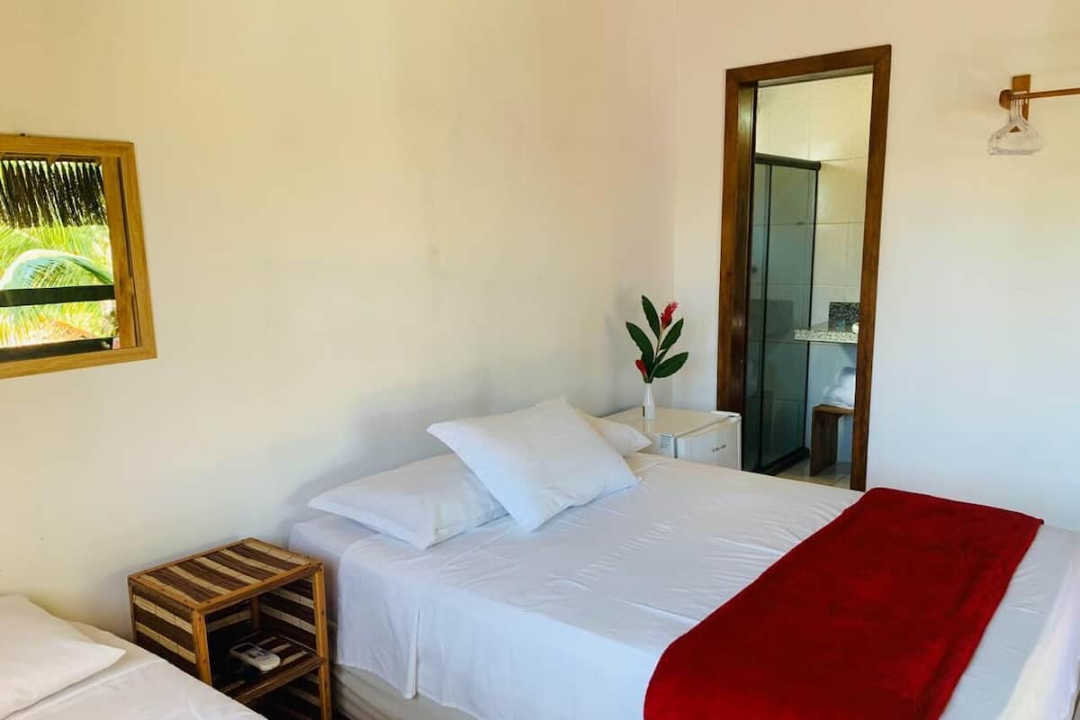 Quarto com uma cama, mesa de cabeceira, pequena mesa de madeira, espelho e janela com vista para o verde.