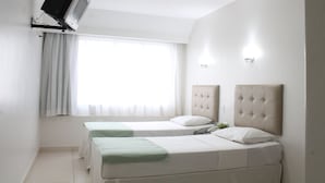 Quarto de hotel com duas camas, televisão de tela plana na parede e uma janela grande com cortinas leves.