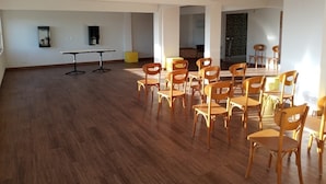 Um quarto amplo com piso de madeira, uma mesa comprida e várias cadeiras dispostas para refeições.