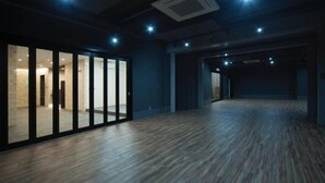 Interior espaçoso e moderno, com piso de madeira, portas de vidro que dão para outro cômodo e iluminação embutida no teto.