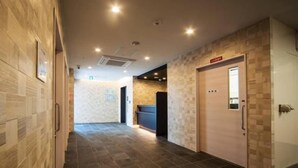 Corredor de hotel com piso de azulejos, área de recepção e uma porta com placa.