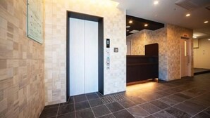 Um saguão de hotel moderno com piso ladrilhado, balcão de recepção e elevador.