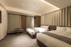 Quarto de hotel com duas camas, uma mesa redonda pequena e um banco.