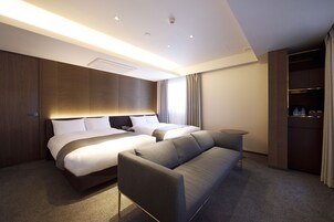Quarto de hotel moderno com duas camas, um sofá, uma pequena mesa e um minibar.