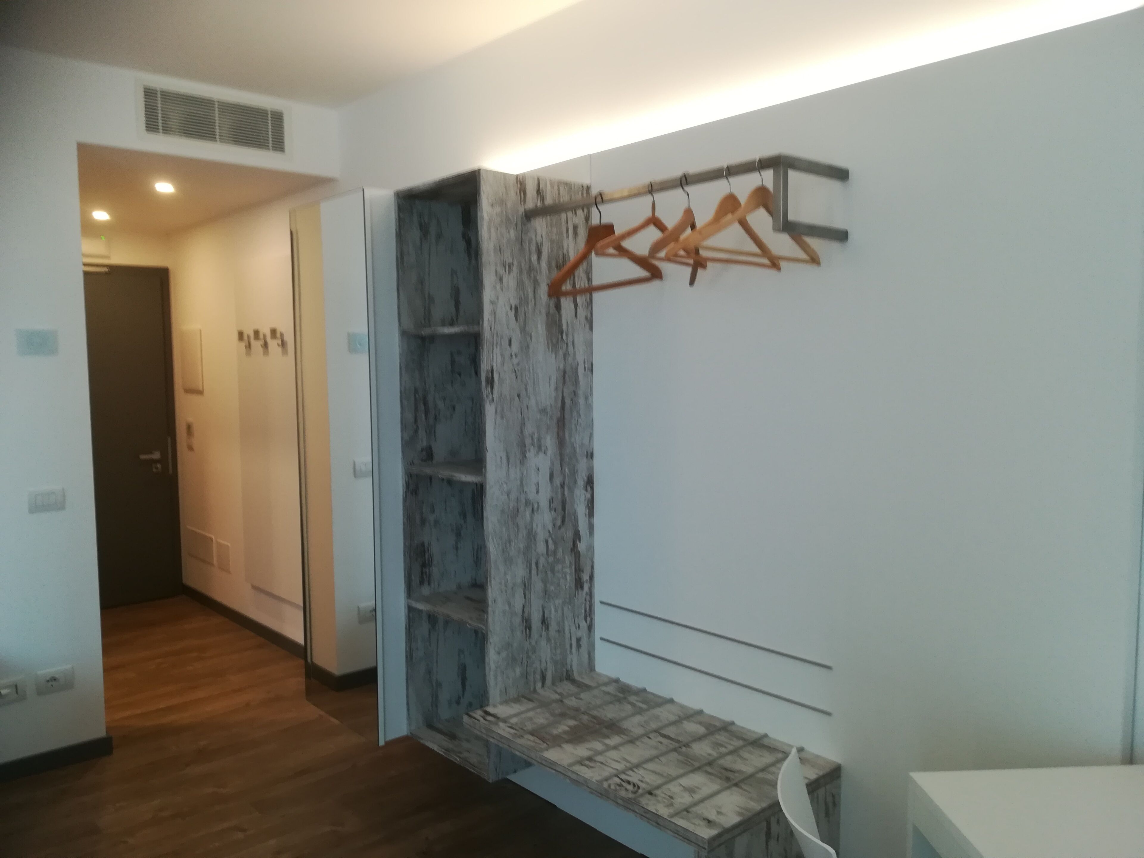 Quarto moderno com guarda-roupa embutido, soalho de madeira e parede branca com cabide fixo.