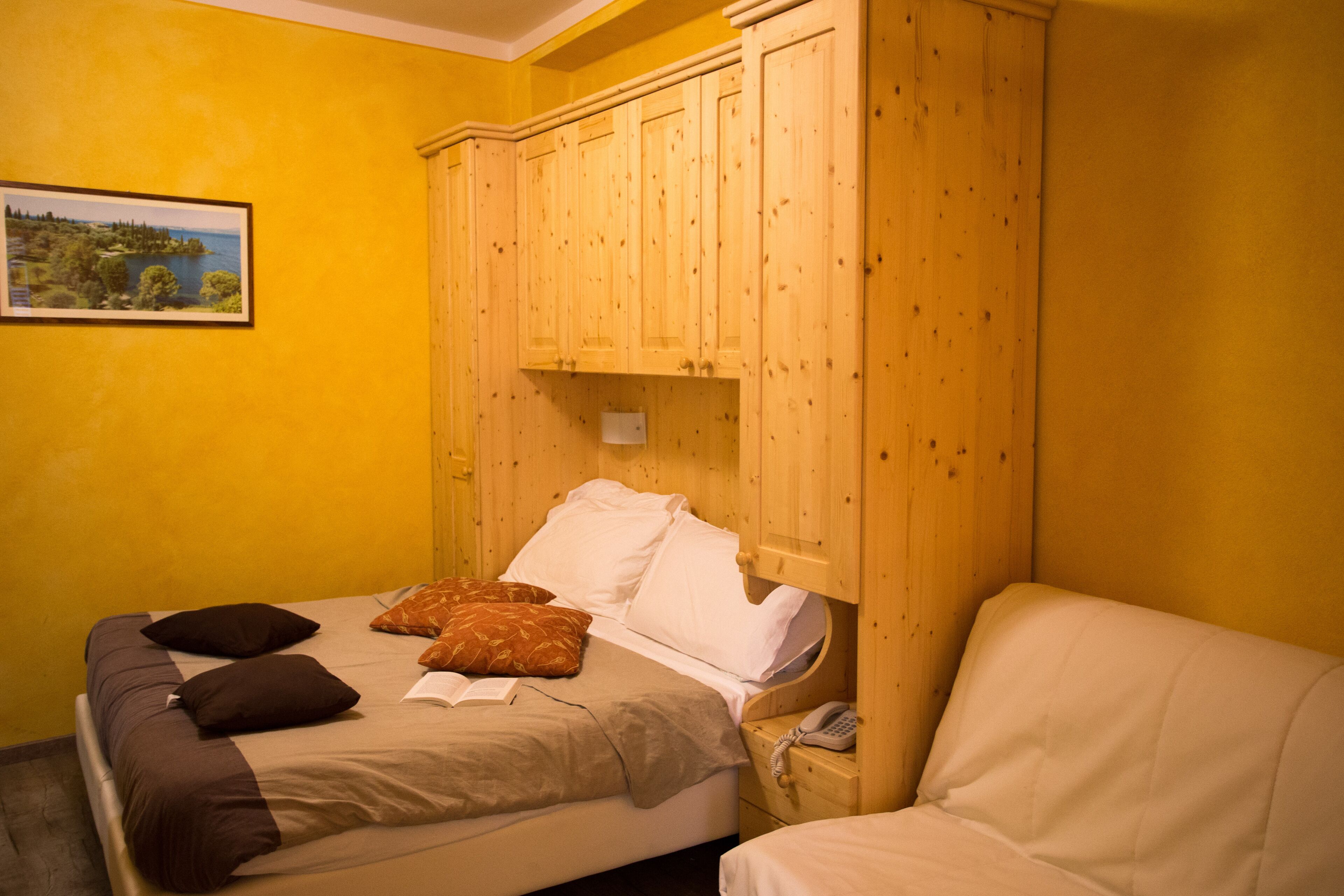 Quarto com uma cama, um guarda-roupa de madeira e uma mesa de cabeceira com um telefone.