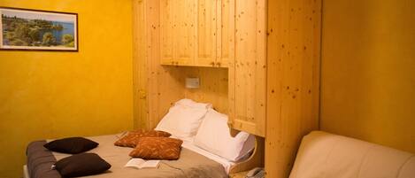 Quarto com uma cama, um guarda-roupa de madeira e uma mesa de cabeceira com um telefone.