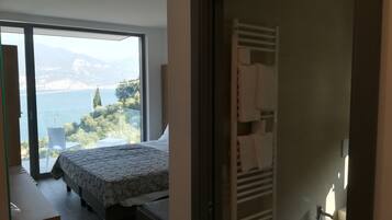 Quarto com cama, mesa de cabeceira e vista para um corpo d'água e montanhas.