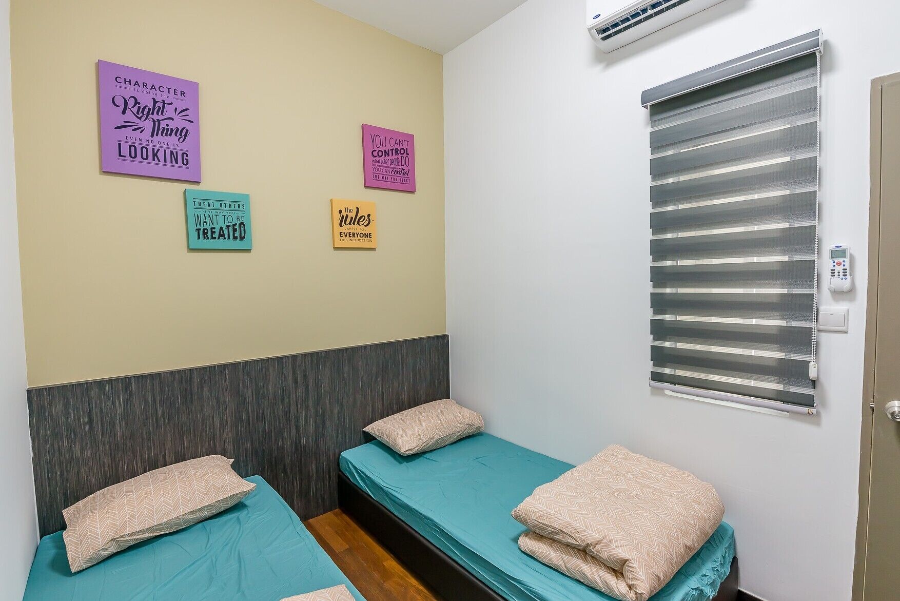 Quarto com duas camas, ar-condicionado fixado na parede e cartazes motivacionais.