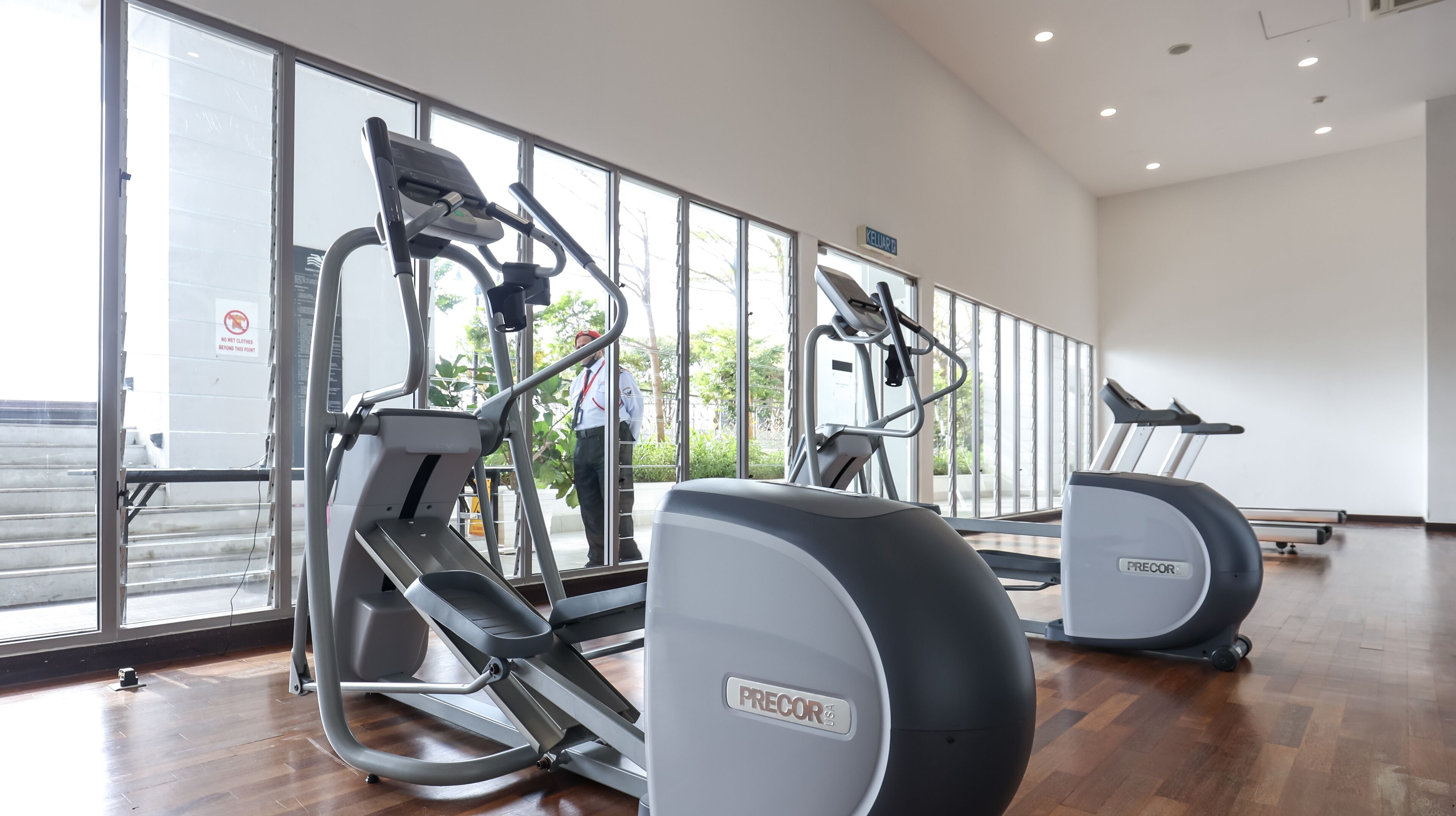 Uma academia com duas máquinas elípticas Precor USA, um espelho e uma janela grande com vista para o exterior.