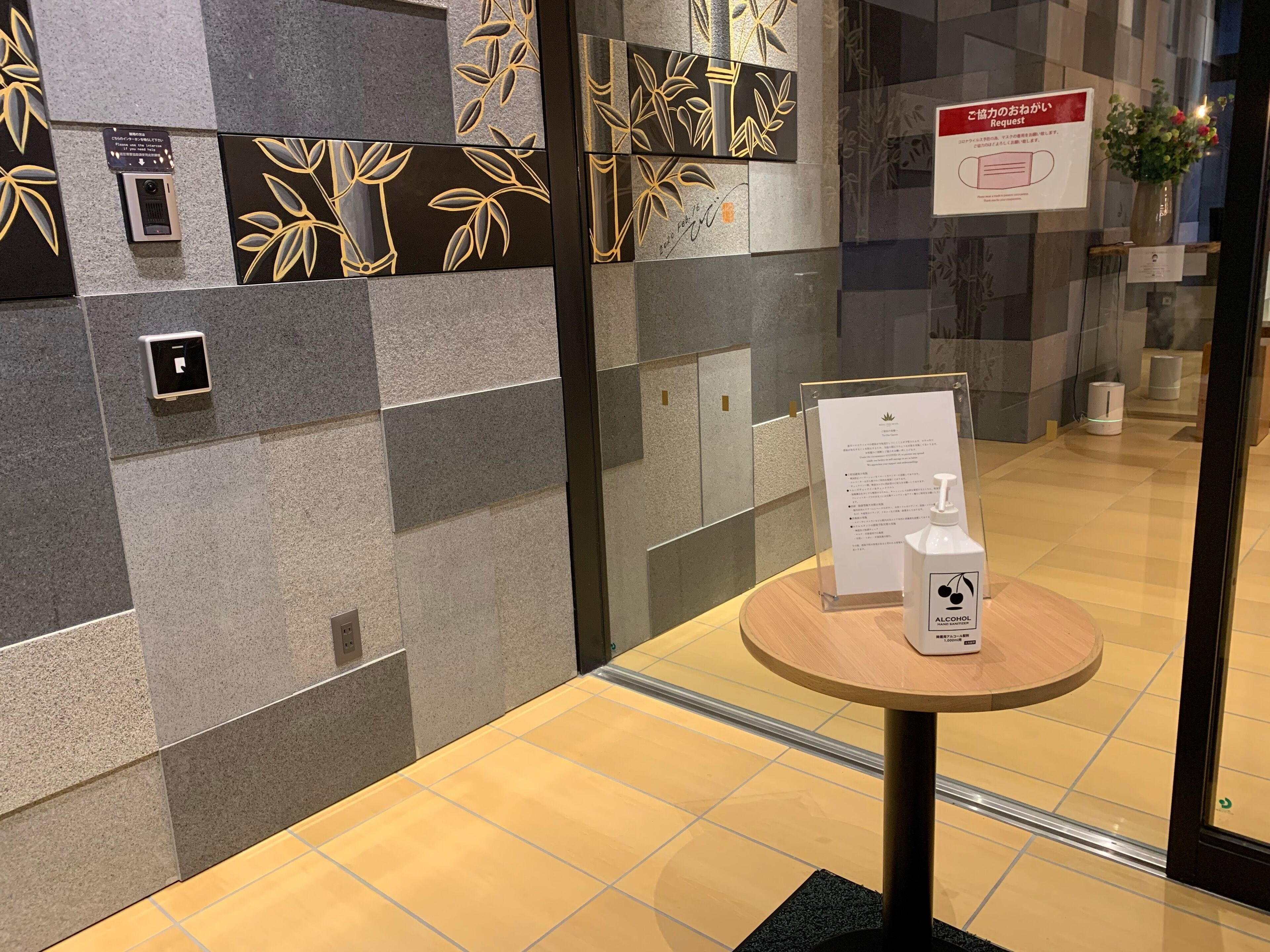 Um saguão moderno com uma mesa de recepção, um quiosque digital de informações e uma pequena mesa com uma garrafa de bebida alcoólica.