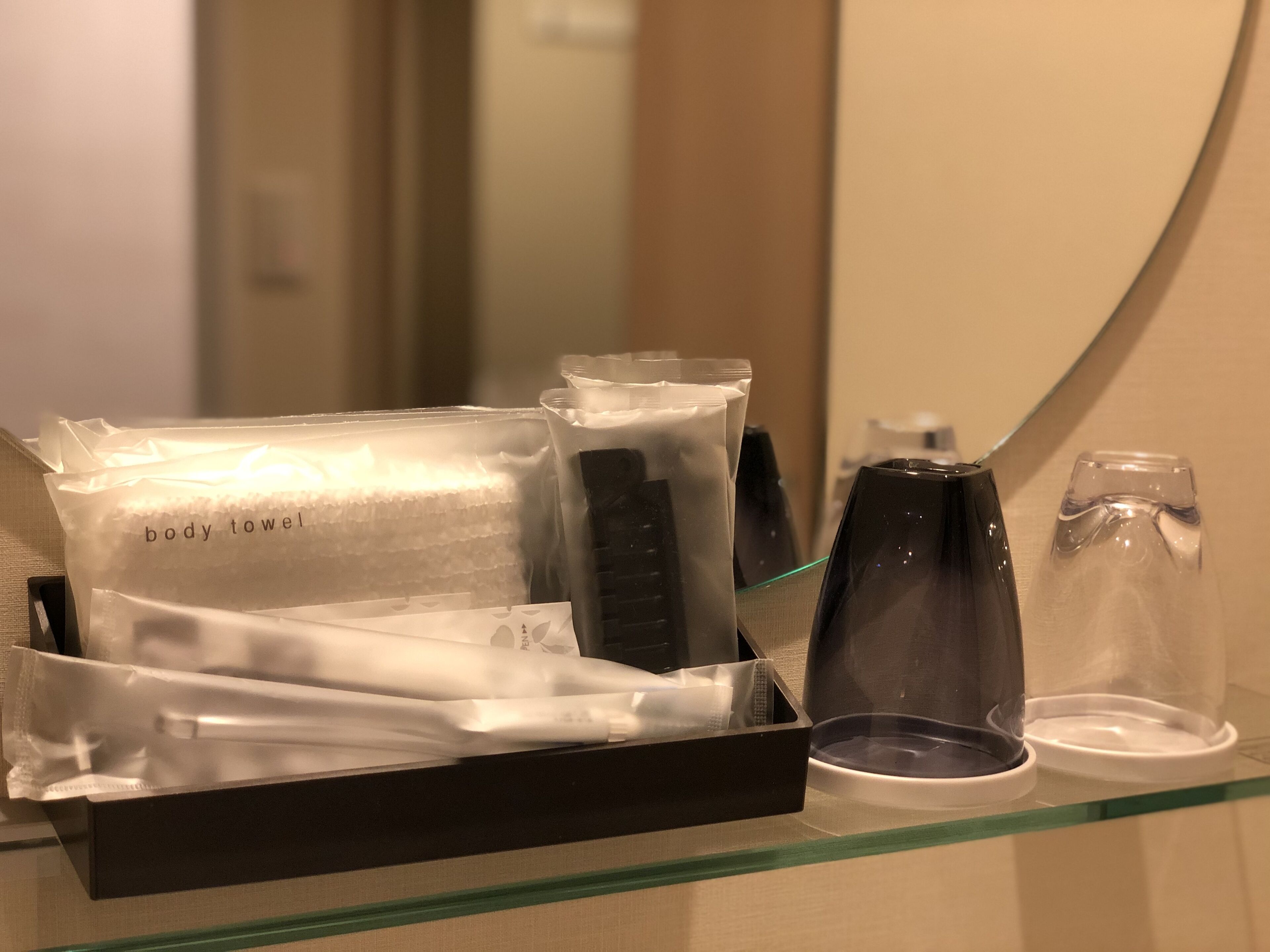 Casa de banho com uma prateleira de vidro que exibe produtos de higiene pessoal, incluindo uma toalha de corpo, um frasco preto e um recipiente transparente.