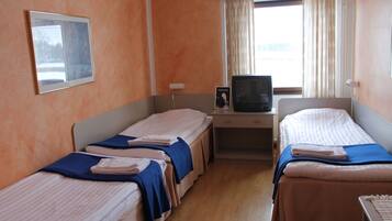 Quarto de hotel com duas camas de solteiro, uma escrivaninha com televisão e uma janela com cortinas.