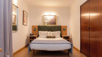 Quarto de hotel com cama, mesas de cabeceira, um guarda-roupa e uma obra de arte na parede.