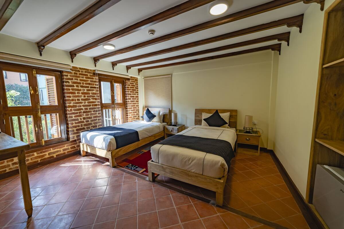 Quarto com duas camas, parede de tijolos, vigas de madeira e uma janela.