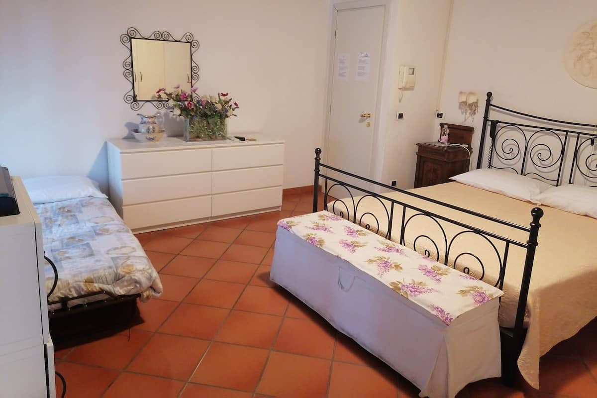 Quarto com duas camas de solteiro, uma cômoda, um espelho e uma mesa pequena com um vaso de flores.