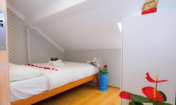 Quarto com uma cama de solteiro, um vaso azul com flores e um guarda-roupa branco.