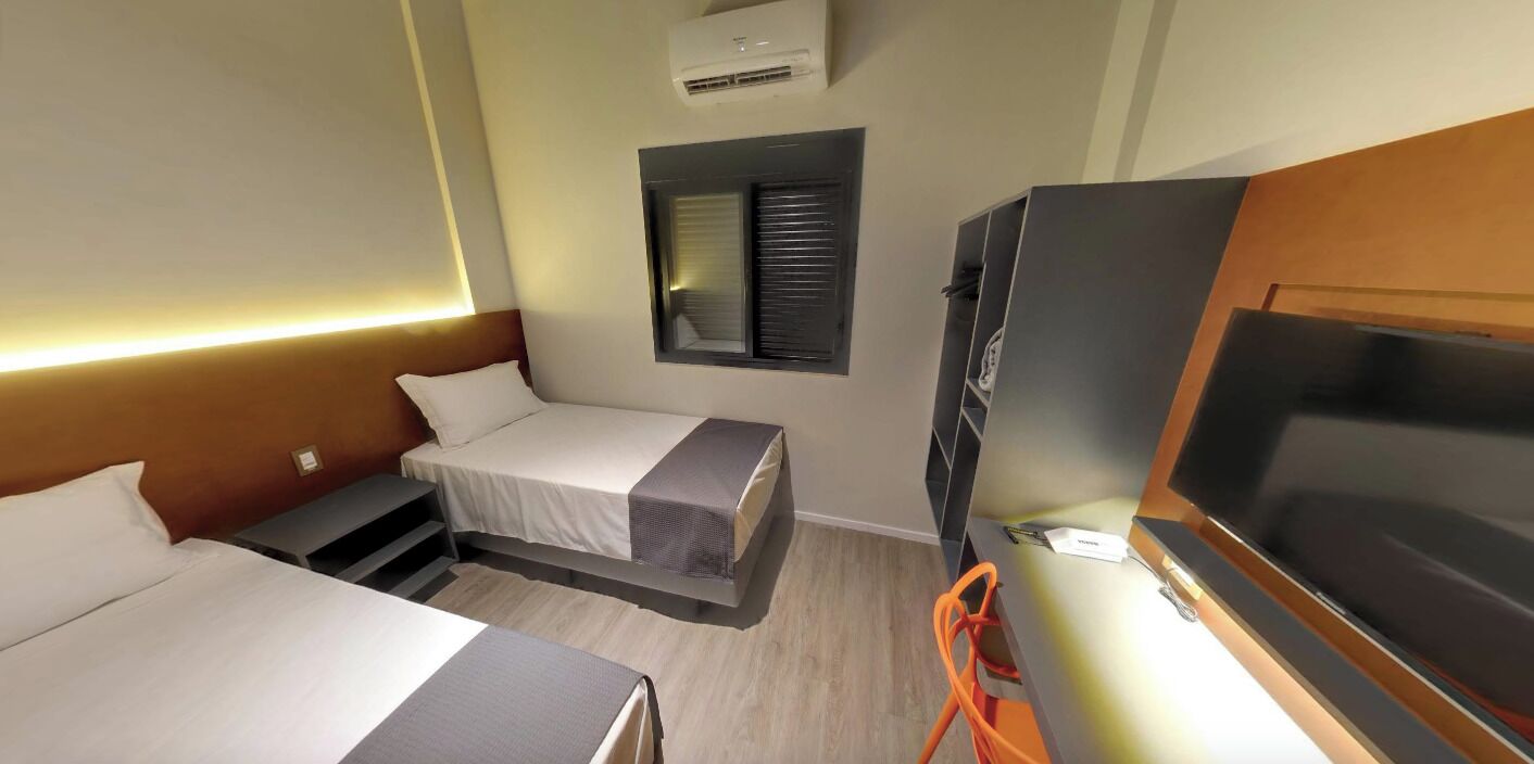 Quarto de hotel com duas camas, televisão e escrivaninha.