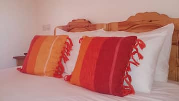 Cama com lençóis brancos e duas almofadas com listras vermelhas e laranja.