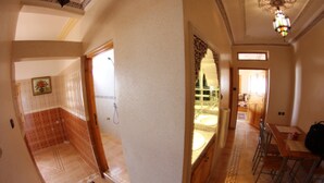 Um corredor com piso de azulejos, porta de madeira, espelho e um espaço de jantar com cadeiras e mesa.