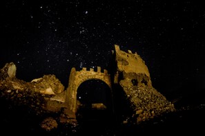 Uma estrutura de pedra histórica com entrada em arco, cercada por escombros sob um céu estrelado.