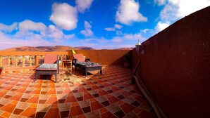 Um pátio com piso de azulejos, móveis de exterior e vista para o deserto ao fundo.