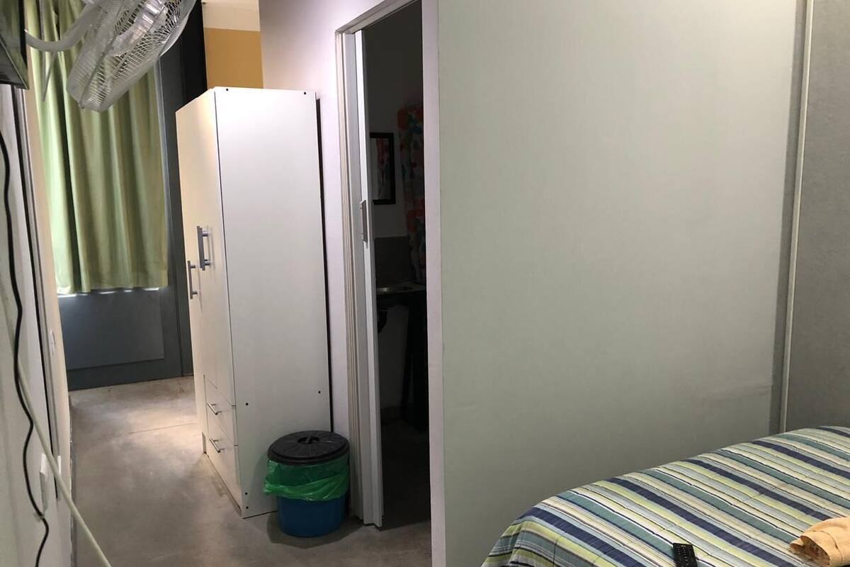 Quarto pequeno e compacto, com cama, armário e lixeira.