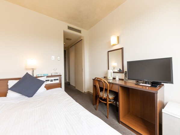 Quarto de hotel com uma cama, uma escrivaninha com cadeira, televisão e banheiro.