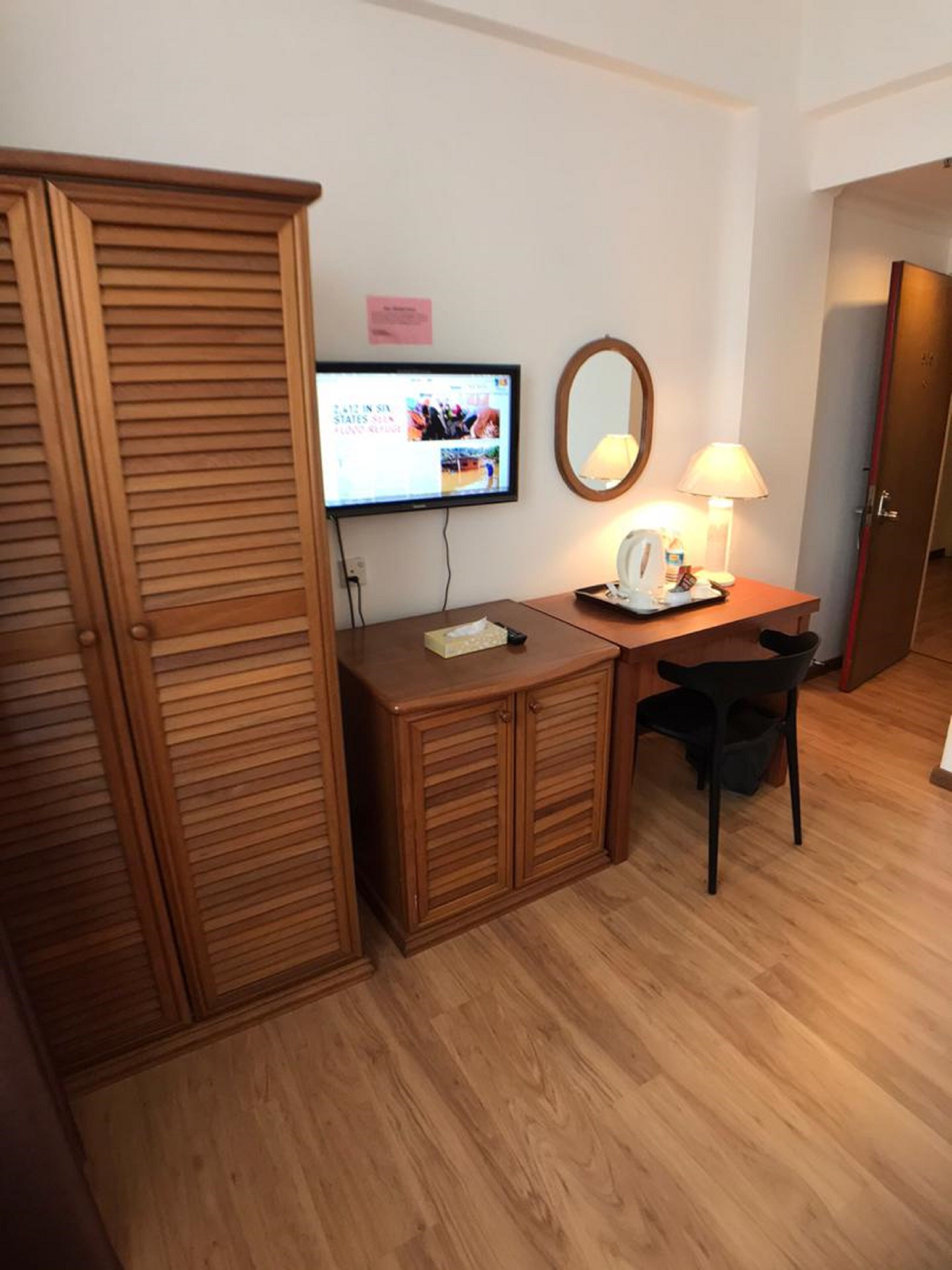 Quarto compacto com guarda-roupa de madeira, escrivaninha com luminária, televisão e espelho.