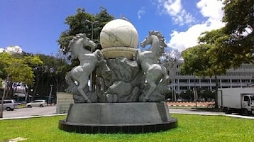 Escultura de dois cavalos com um globo em suas costas, posicionada sobre uma base circular em uma área gramada.
