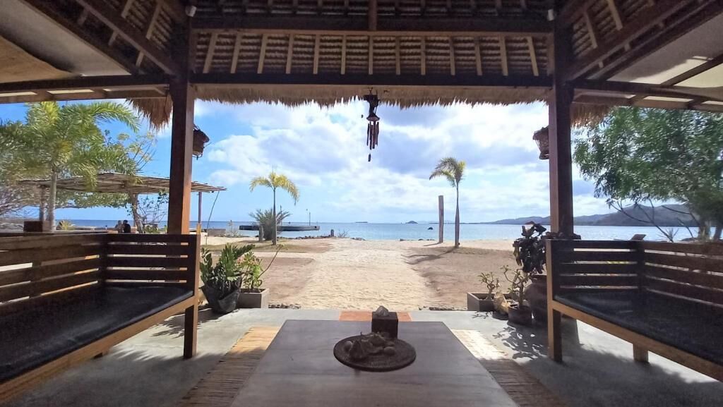 Vista da praia a partir de uma área coberta com bancos e uma pedra decorativa.