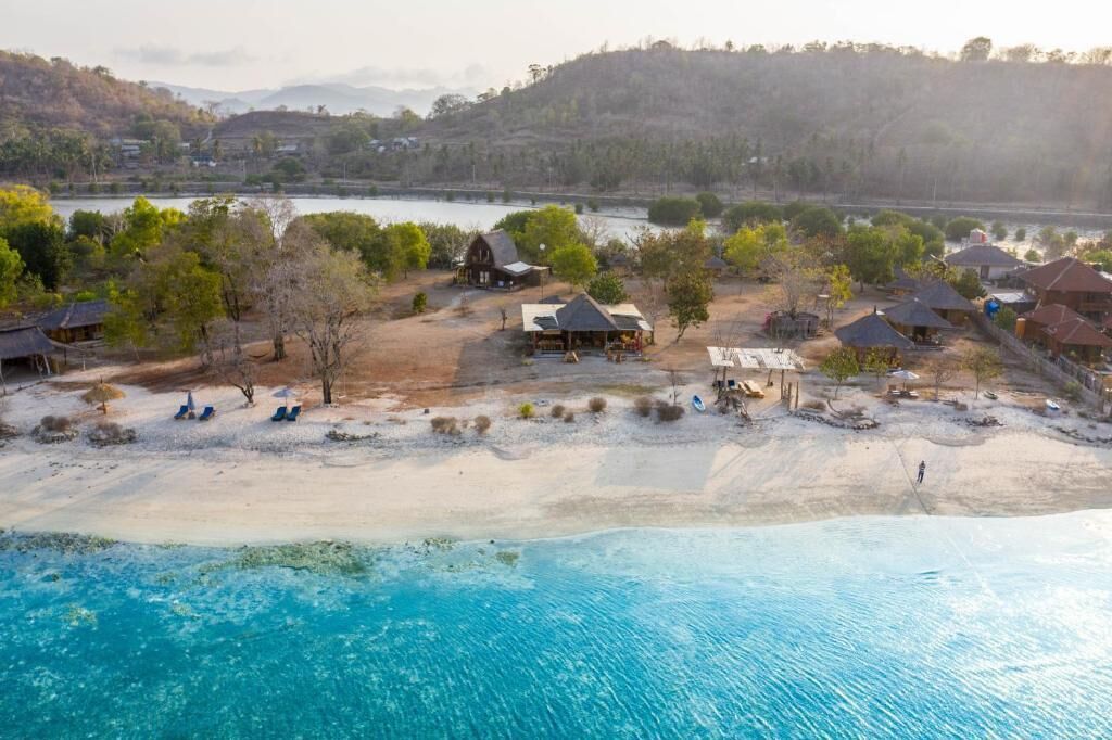 Uma área costeira com praia, um pequeno povoado com casas e um corpo d'água ao fundo.