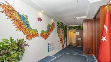 Um corredor com um mural colorido de asas, uma bandeira turca e um letreiro com ícones de redes sociais.