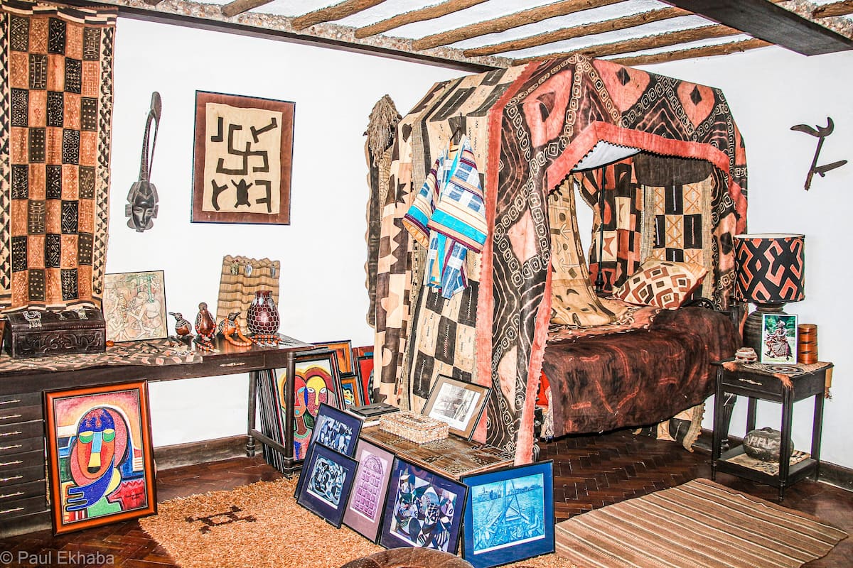 Quarto com cama coberta por mantas estampadas, cabeceira de madeira e uma mesinha com objetos decorativos.